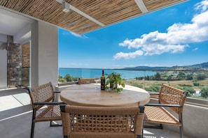 Mesa redonda com cadeiras de vime, uma garrafa de vinho e uma planta em uma varanda com vista para uma paisagem deslumbrante.