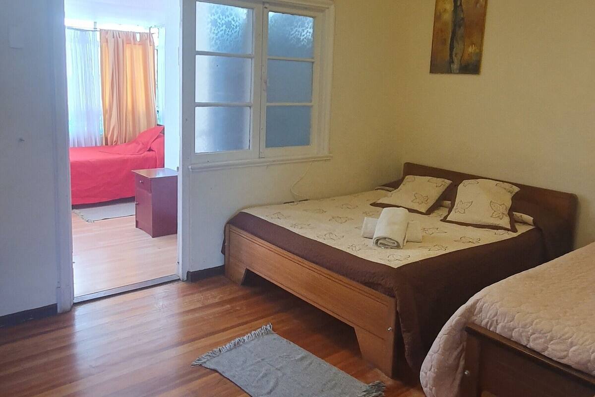 Quarto com duas camas, piso de madeira, porta que dá para uma varanda e um quadro na parede.