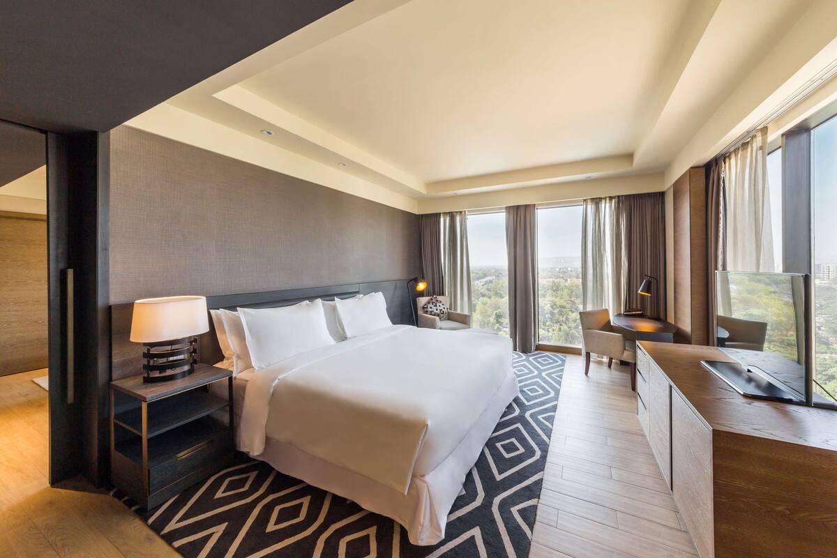 Quarto de hotel moderno com uma cama grande, uma mesa de trabalho e vista para a cidade.
