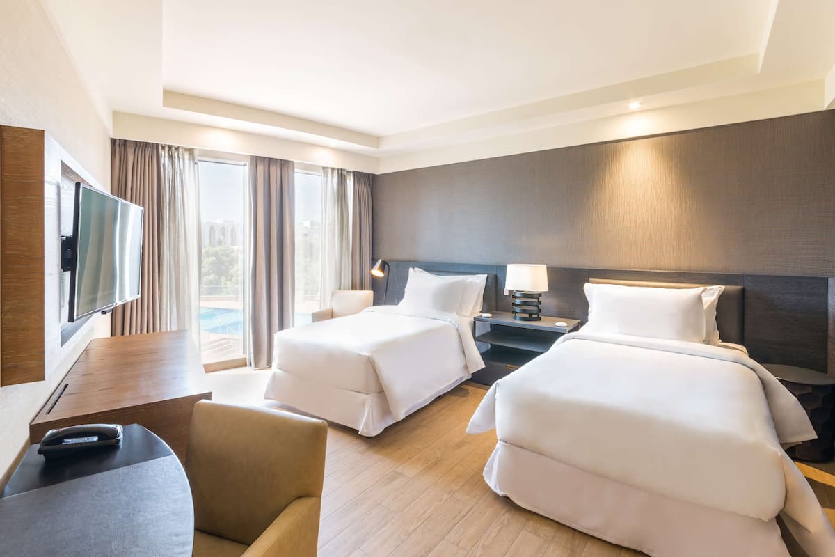 Quarto de hotel com duas camas, uma mesa, televisão de tela plana, uma cadeira e vista para o exterior.