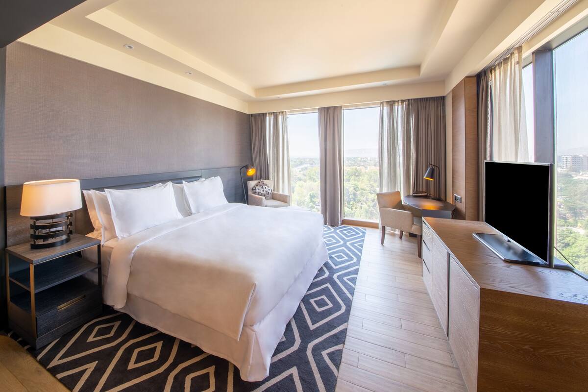 Quarto de hotel moderno com uma cama grande, uma escrivaninha e uma televisão.