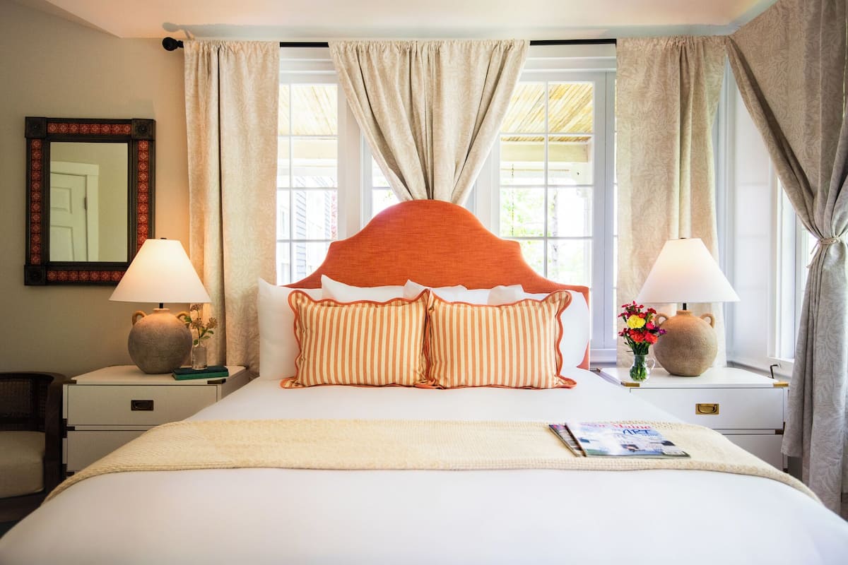 Quarto de hotel com uma cama grande, duas mesas de cabeceira com luminárias, um espelho e cortinas.