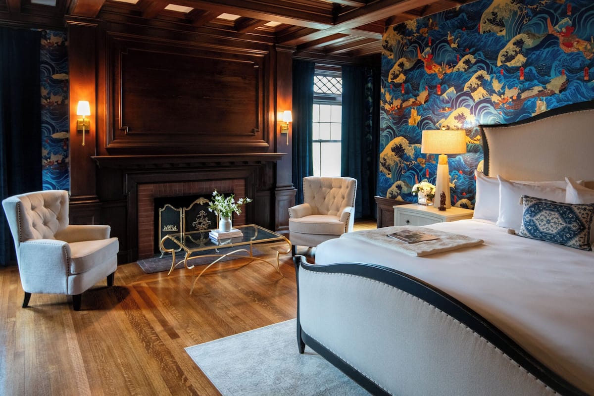 Quarto com cama grande, duas poltronas, lareira e arte tradicional japonesa nas paredes.
