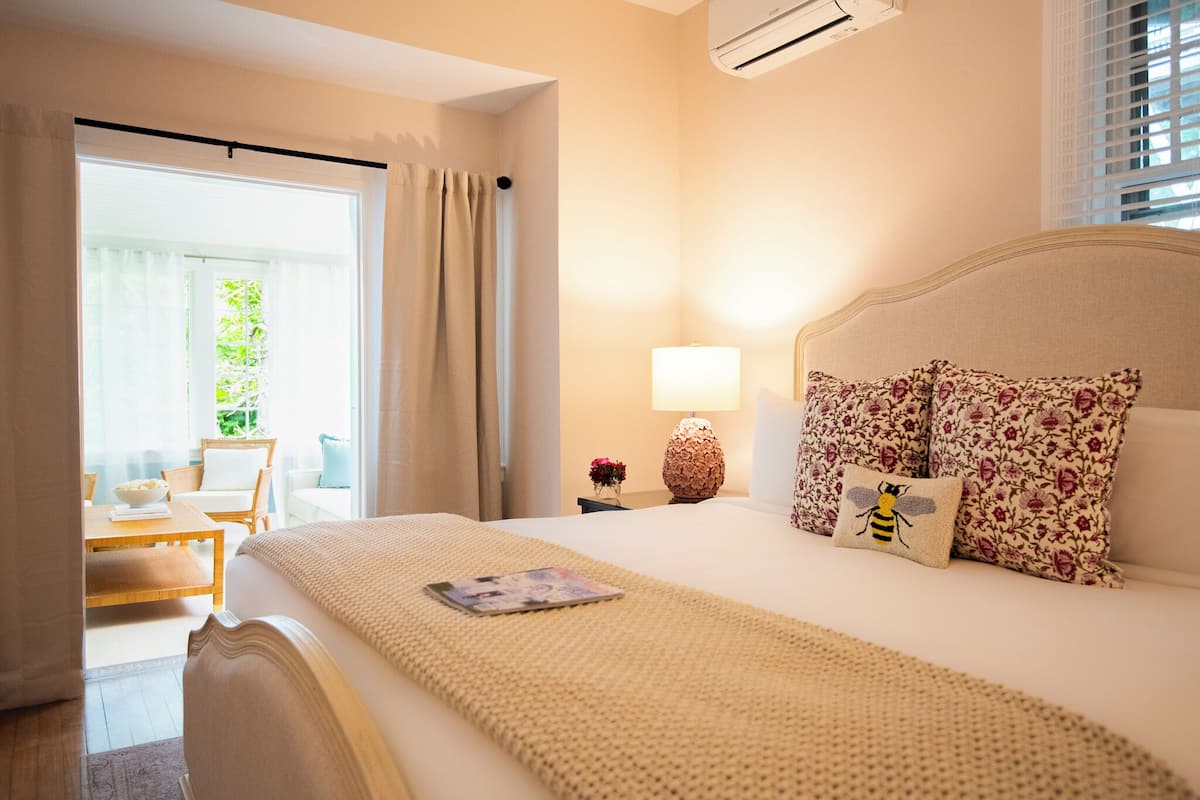 Quarto de hotel com cama, mesa de cabeceira, luminária, janela com cortinas e vista para o exterior.