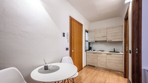 Cozinha compacta com uma mesa branca, duas cadeiras brancas e armários de madeira clara.