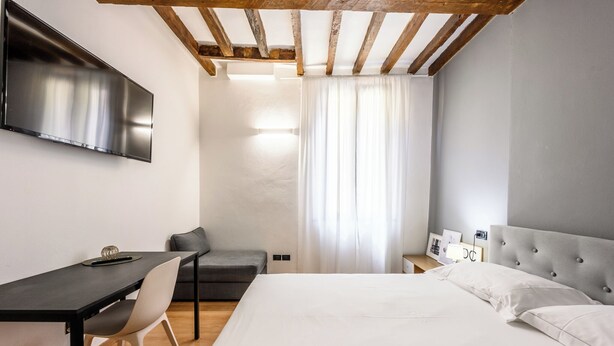 Quarto de hotel com cama, escrivaninha, cadeira, televisão e janela com cortinas.