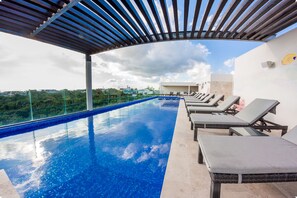 Uma piscina infinita com espreguiçadeiras e um pergolado.
