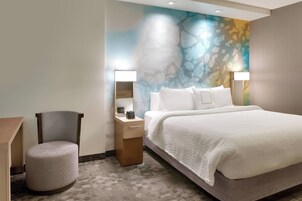Quarto de hotel com cama, poltrona, escrivaninha e mesa de cabeceira.