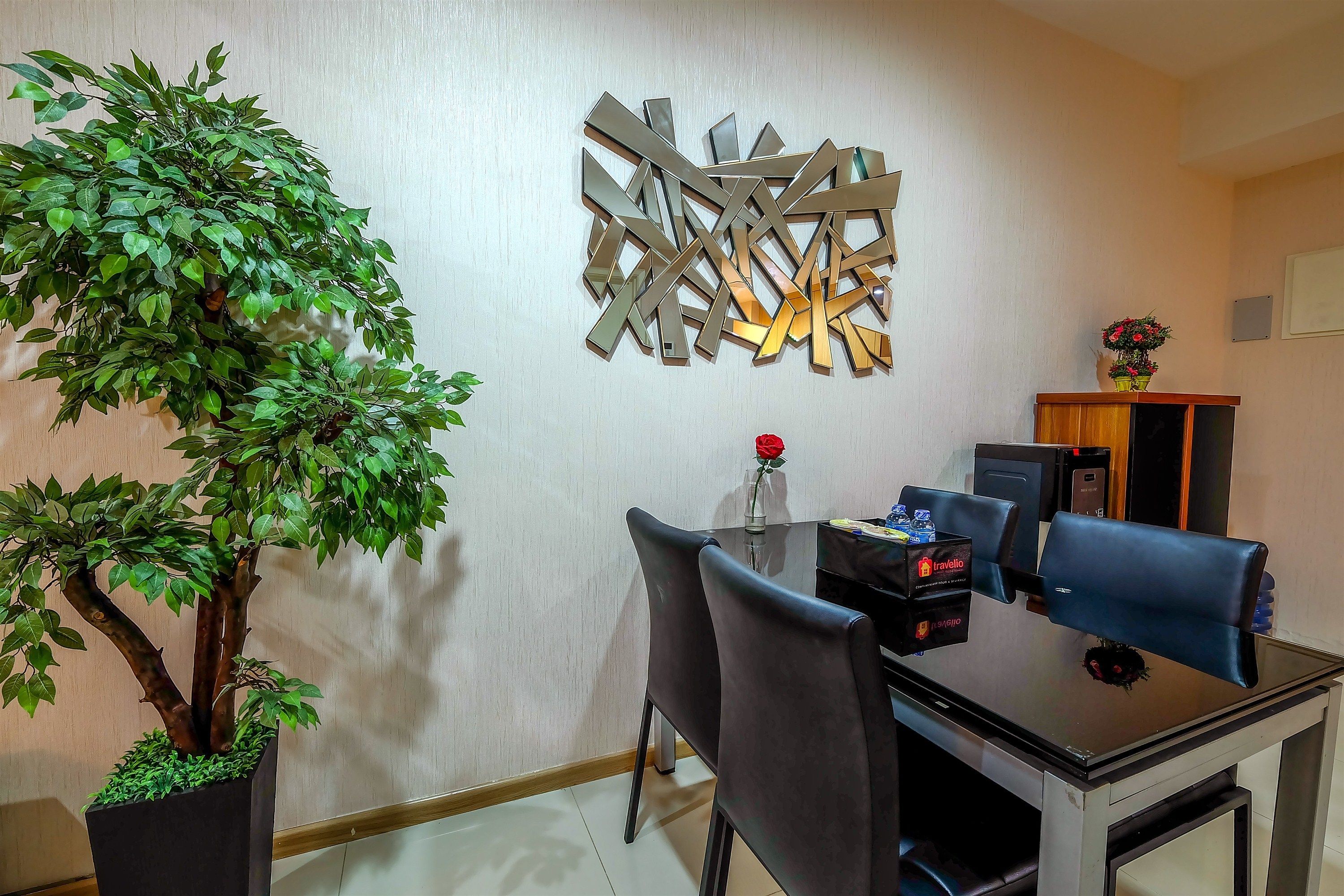 Uma sala de jantar com uma mesa, cadeiras, um painel decorativo, uma planta em vaso e um pequeno armário com um vaso.