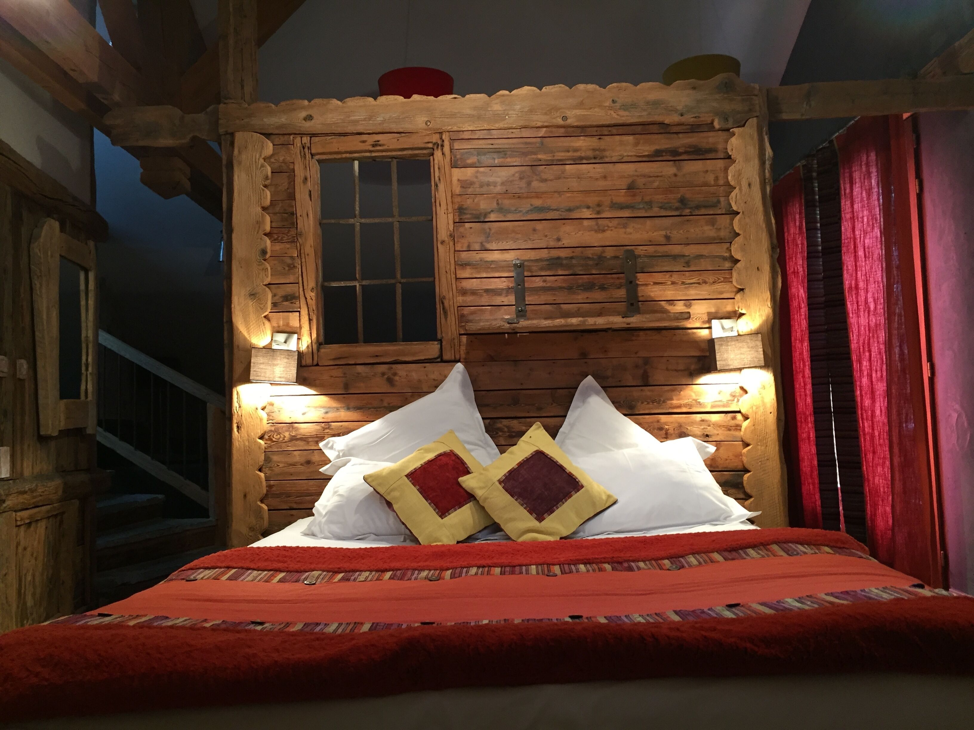 Um quarto estilo cabana de madeira com uma cama, duas almofadas e um cobertor vermelho.