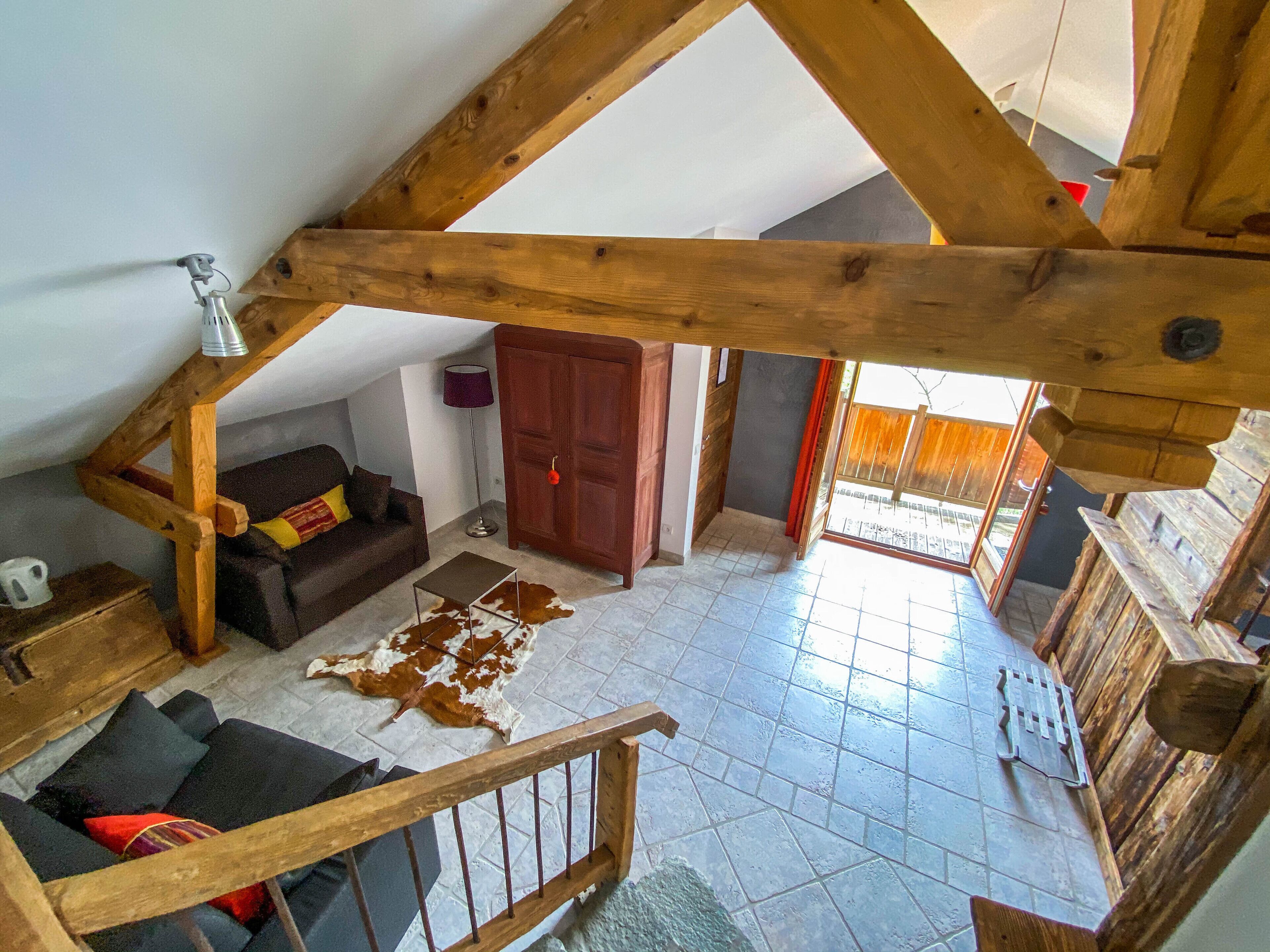 Um amplo loft com pé direito alto, vigas de madeira aparentes, um sofá de couro, uma mesa pequena e vista para o exterior.