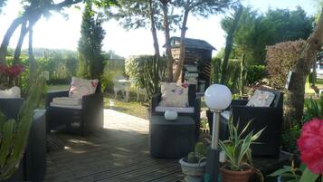 Um pátio externo com móveis de vime, uma mesa pequena e plantas em vasos.
