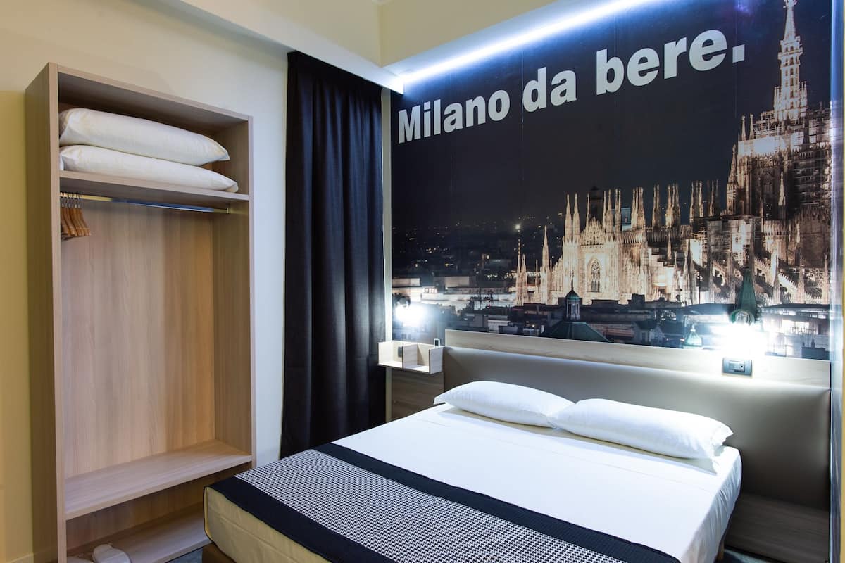 Quarto de hotel com cama, guarda-roupa e pôster de paisagem urbana.