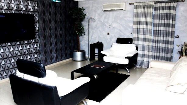 Uma sala de estar moderna com um sofá preto e branco, uma mesa de centro, uma TV fixada numa parede com padrão geométrico e um vaso de planta.