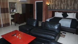 Quarto de hotel com cama, escrivaninha, mesa de centro vermelha e dois sofás de couro preto.