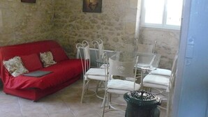 Quarto com sofá vermelho, cadeiras brancas e uma pequena mesa. Há duas pinturas na parede.