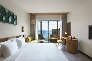 Quarto de hotel com uma cama grande, uma escrivaninha, uma cadeira, uma mesinha e varanda com vista para o mar.