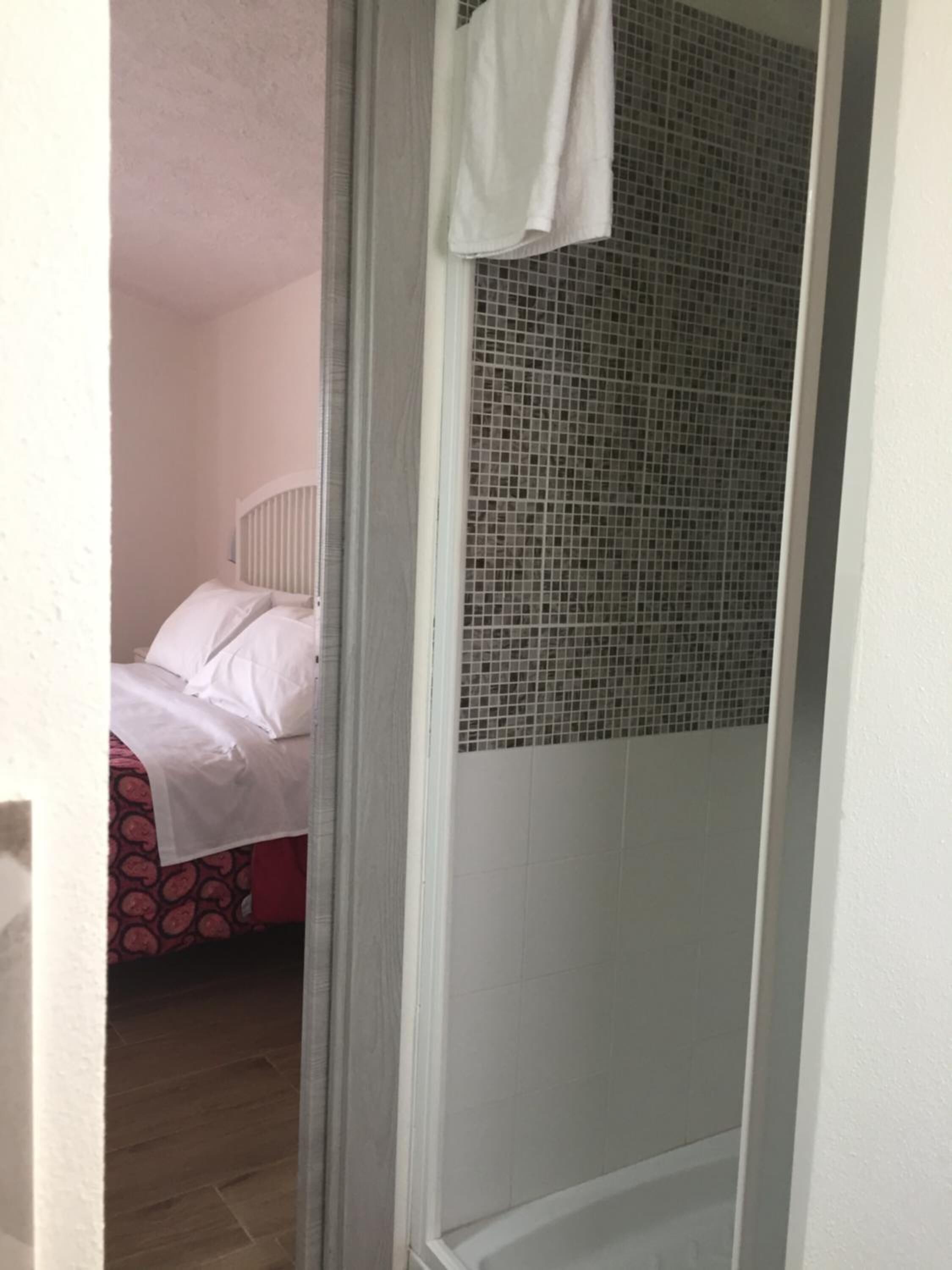 Quarto com cama, área de chuveiro com parede azulejada e cortina branca.