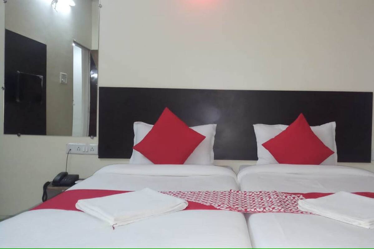 Cama de casal com roupa de cama branca e vermelha, cabeceira preta e mesa de cabeceira com telefone.