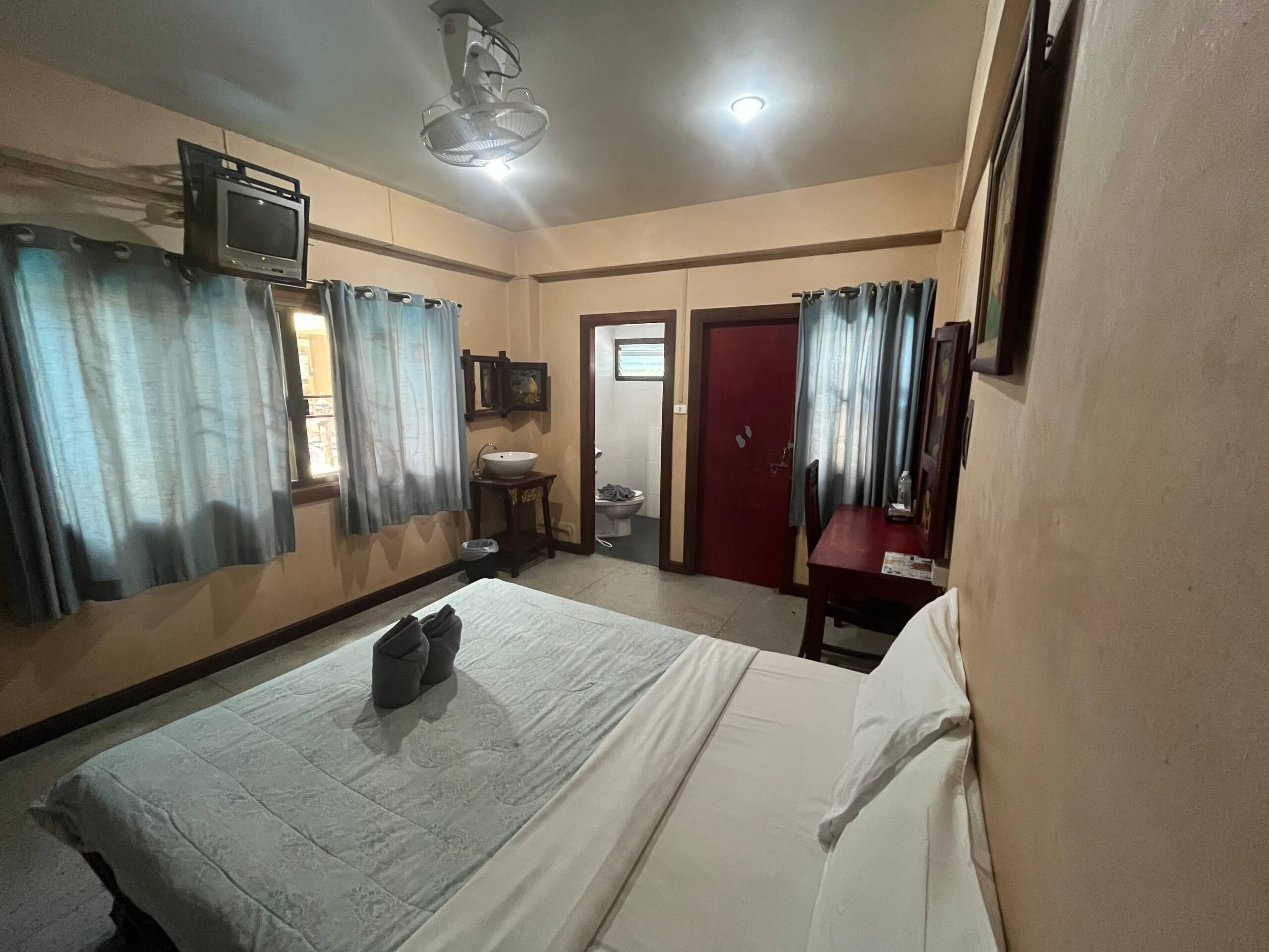 Quarto de hotel com uma cama, televisão presa na parede, pia e porta para o banheiro.