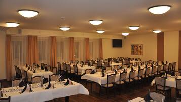 Uma sala de banquetes com várias mesas montadas para refeições, dispostas em fileiras, e equipada com cadeiras.