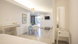 Quarto de hotel moderno com cama, escrivaninha, cadeira, mesa de jantar com cadeiras, mesinha com espelho e televisão na parede.