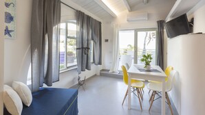 Quarto com cama, mesa de jantar com cadeiras, televisão e janela com cortinas.