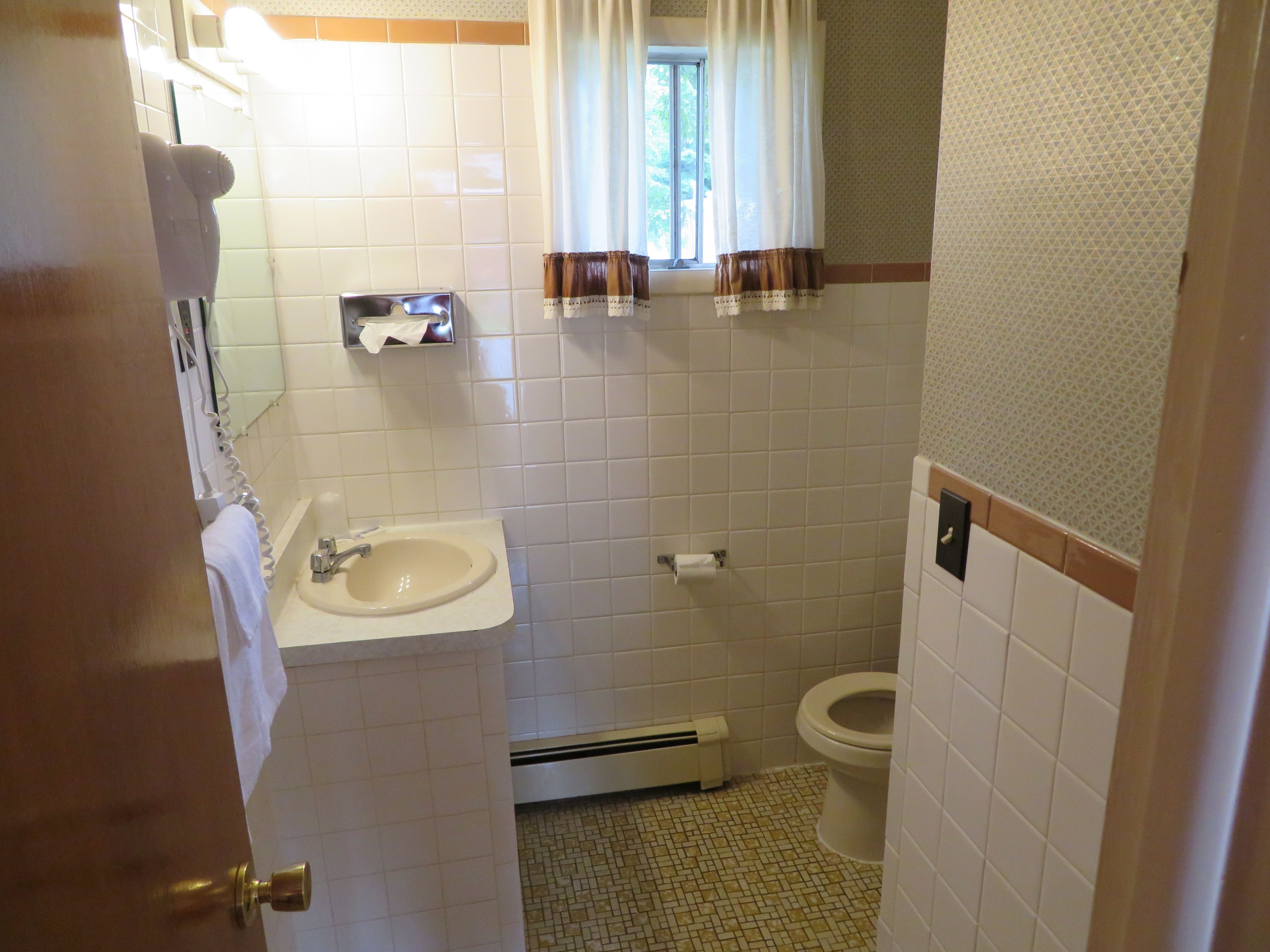 Casa de banho compacta com lavatório, sanita e janela com cortinas.