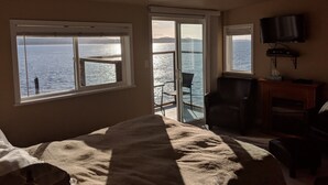 Quarto com cama, poltrona, televisão e vista para o mar por uma porta de correr.