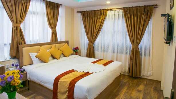 Quarto de hotel com uma cama grande, cortinas, uma mesinha de cabeceira e um vaso de flores.