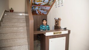 Uma receção com uma placa a indicar 'RECEPTION' e uma escadaria que leva a um quarto com cama e janela.