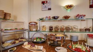 Buffet com diversos alimentos, incluindo queijos, frutas e pratos prontos, sobre um balcão de mármore.