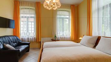 Quarto de hotel com cama, sofá, televisão e janela com cortinas.