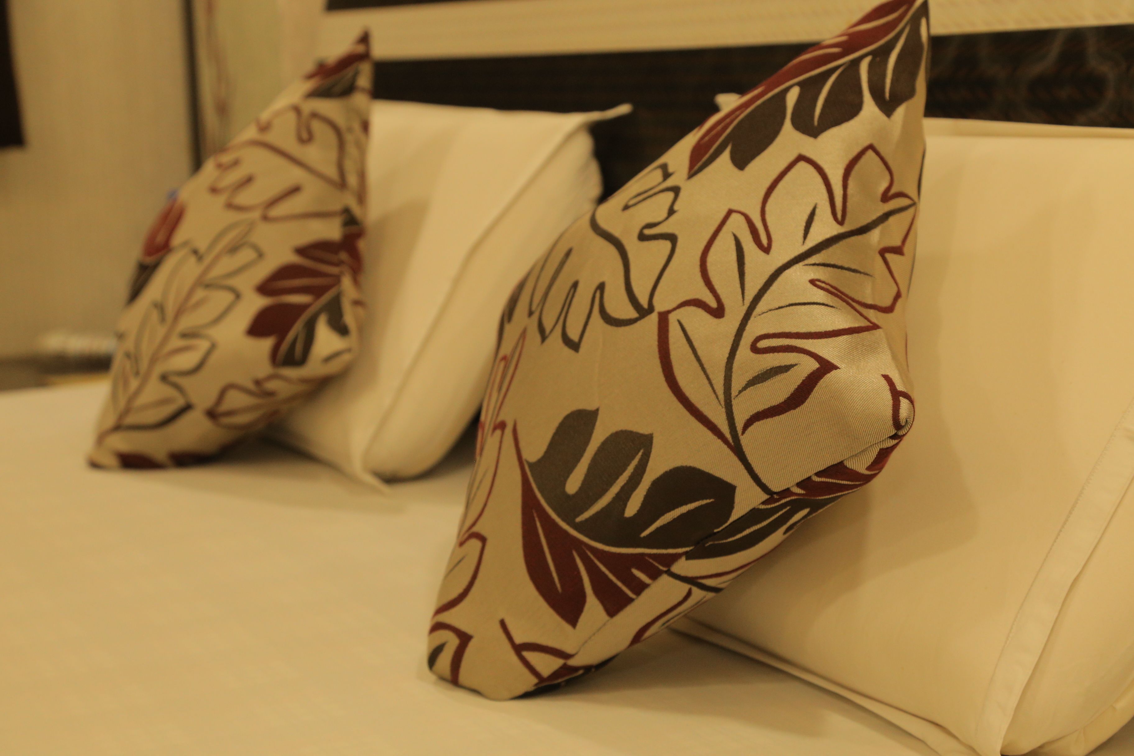 Close-up de duas almofadas decorativas com padrão de folhas sobre uma cama.