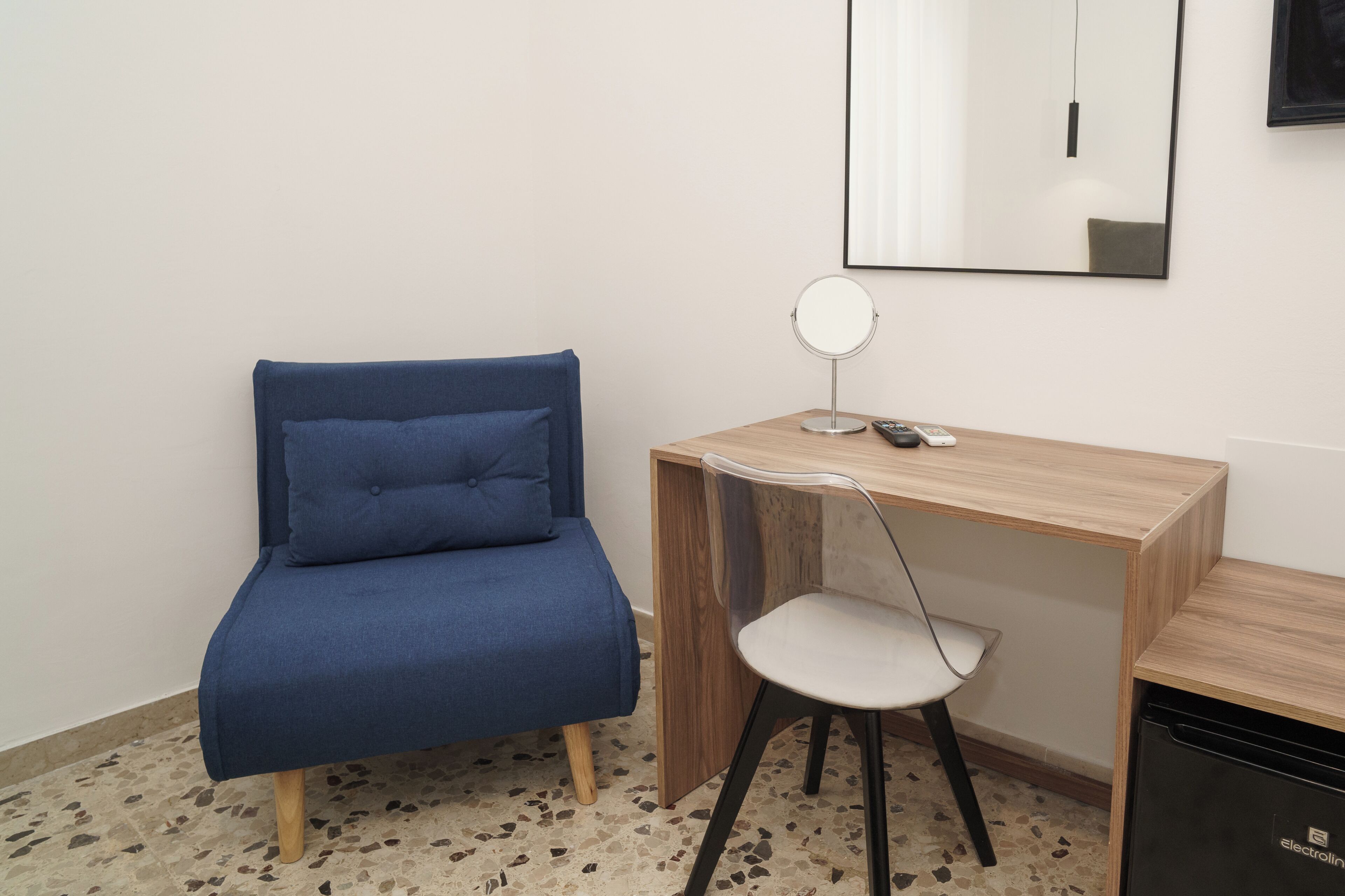 Um quarto com um sofá azul, uma escrivaninha de madeira com um espelho e uma cadeira.