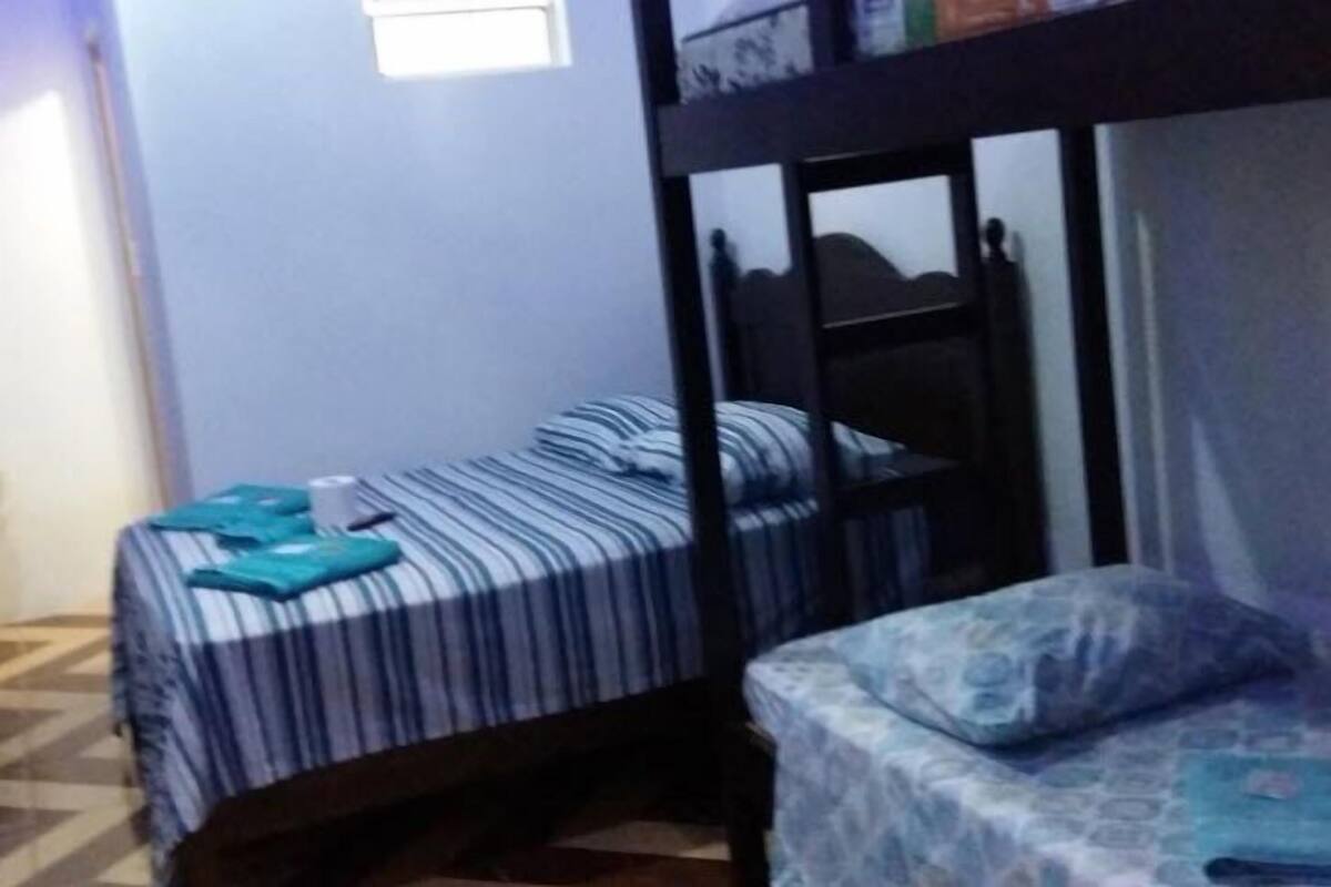 Quarto com duas beliches, uma janela pequena e piso estampado.