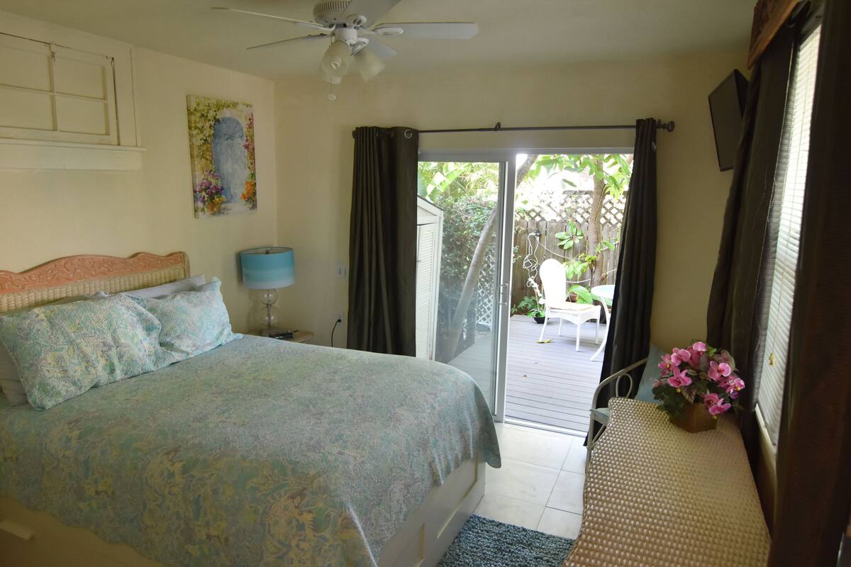 Quarto com cama, ventilador de teto, janela com cortinas e vista para o exterior.