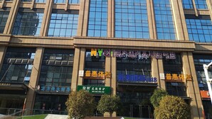 Um edifício alto com vários andares, exibindo uma placa de hotel em destaque e diversos estabelecimentos comerciais no térreo.