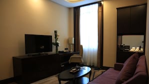 Quarto de hotel moderno com televisão de tela plana, sofá, mesa de centro e escrivaninha com abajur.