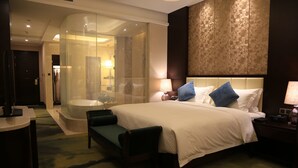 Quarto de hotel com uma cama grande, área de estar, chuveiro em cabine de vidro e banheiro separado.