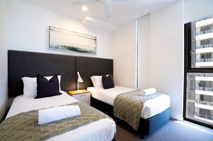 Quarto de hotel com duas camas, um ventilador de teto, uma janela grande e um quadro na parede.