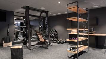 Uma academia com equipamento de musculação, um banco e uma estante de madeira.