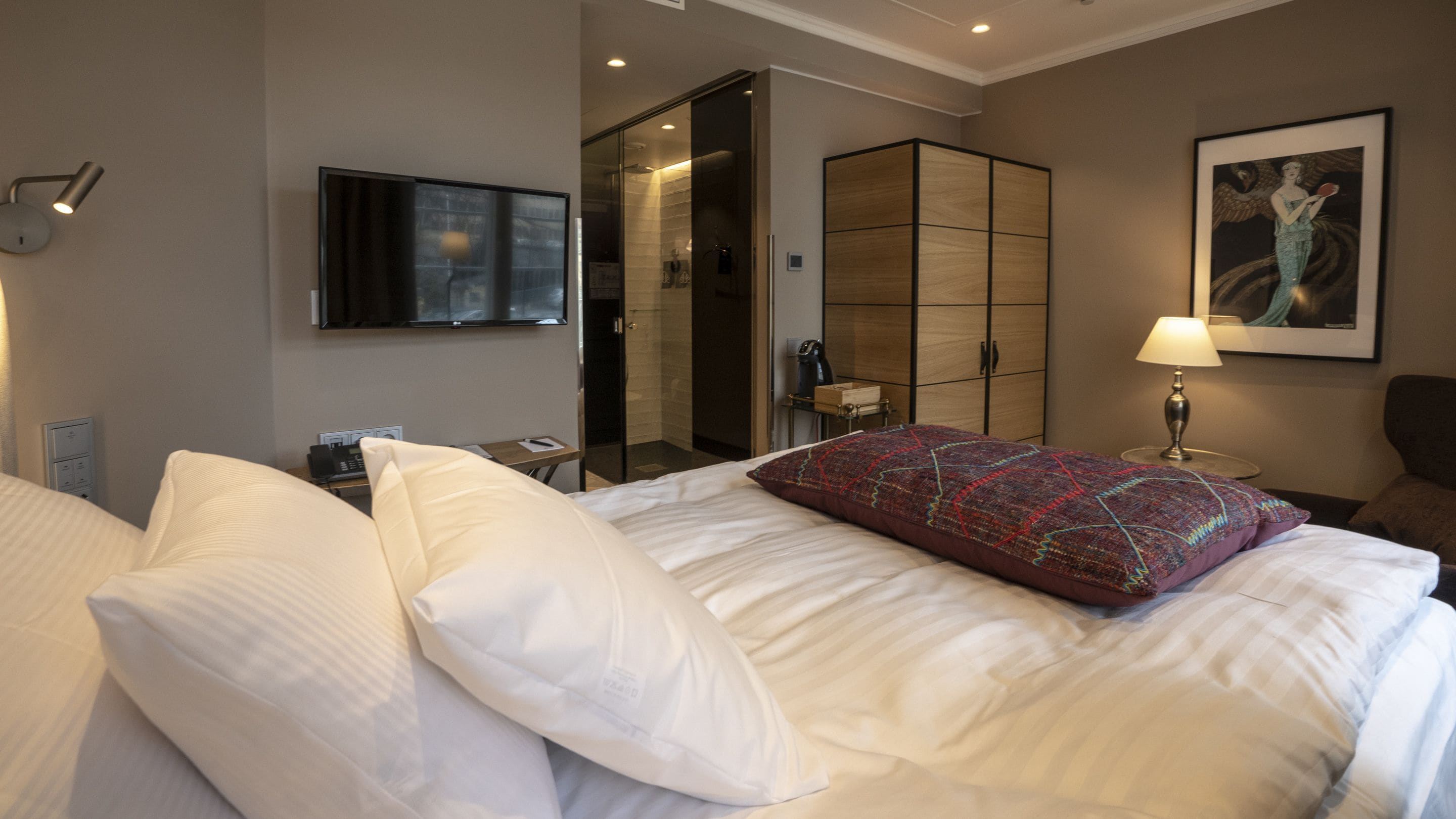 Quarto de hotel com uma cama grande, televisão fixada na parede, guarda-roupa e um quadro na parede.