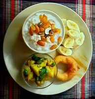 Um prato com uma tigela de aveia coberta com nozes e frutas secas, bananas fatiadas, um alimento frito e uma pequena tigela de um prato com legumes verdes.