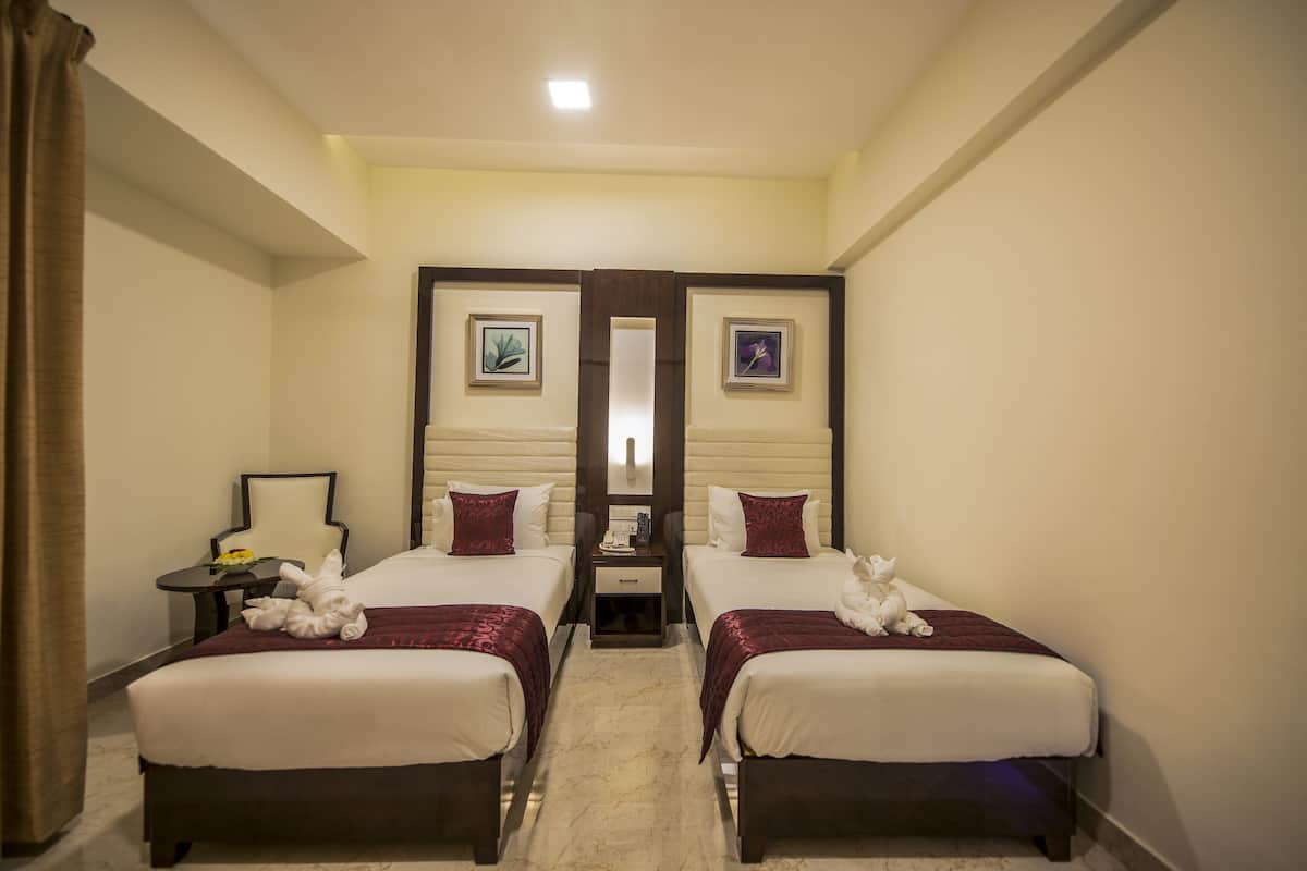 Quarto de hotel com duas camas, uma mesinha com abajur, espelho e quadros nas paredes.