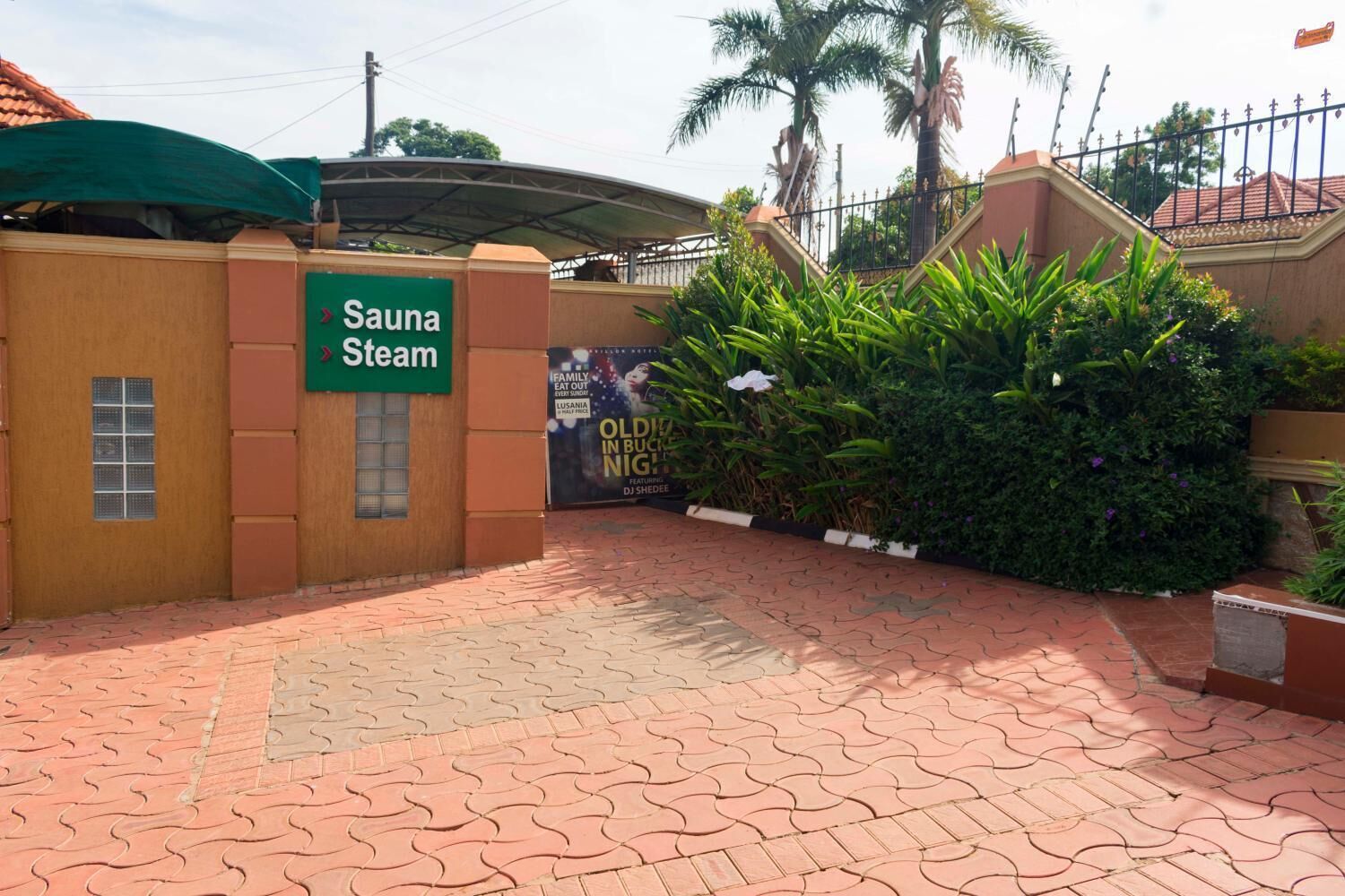 Entrada de um spa com uma placa indicando 'Sauna Steam', calçada e um cartaz publicando um evento musical.