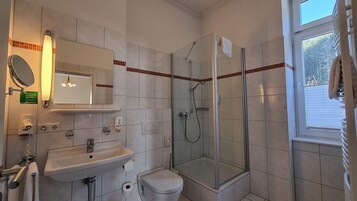 Casa de banho com lavatório, espelho, sanita e cabine de duche.