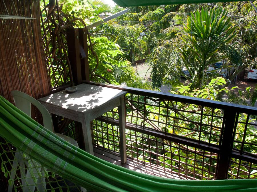 Varanda com vista para um jardim exuberante, uma mesa pequena e uma rede.
