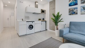 Uma cozinha moderna com eletrodomésticos embutidos, máquina de lavar e um sofá cinzento.