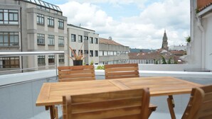 Mesa e cadeiras de madeira numa varanda com vista para a paisagem urbana, incluindo uma torre de igreja.